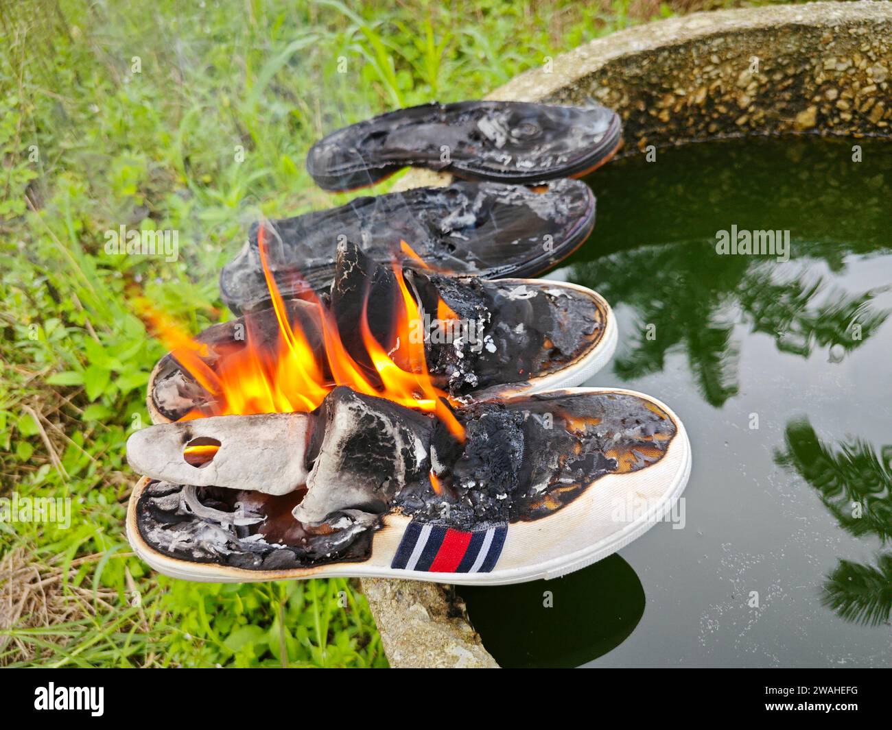 old thrown away shoes on flame by the edge of the cylindrical concrete ...
