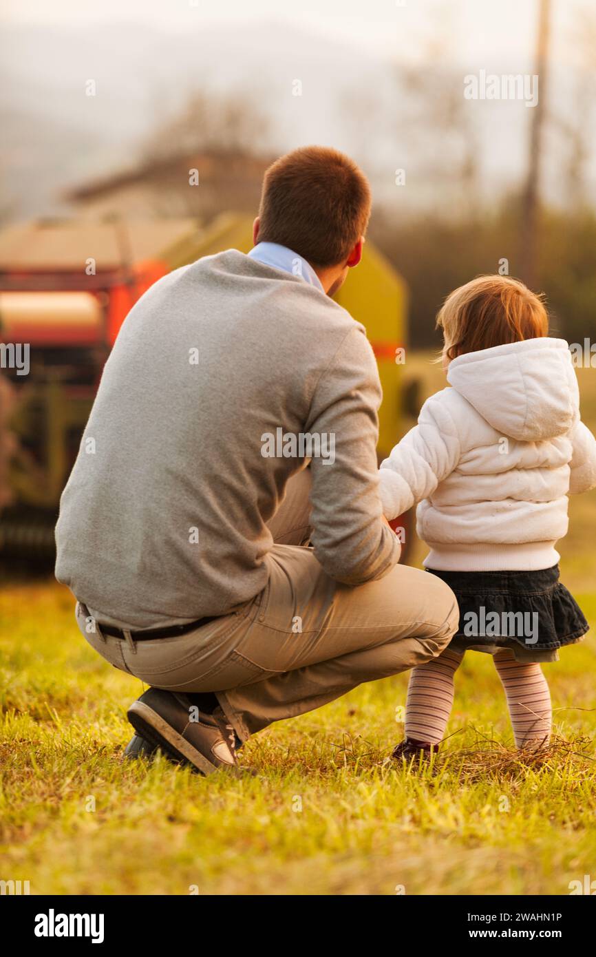 Squatting in the grass, a man engages with his young child, fostering a ...