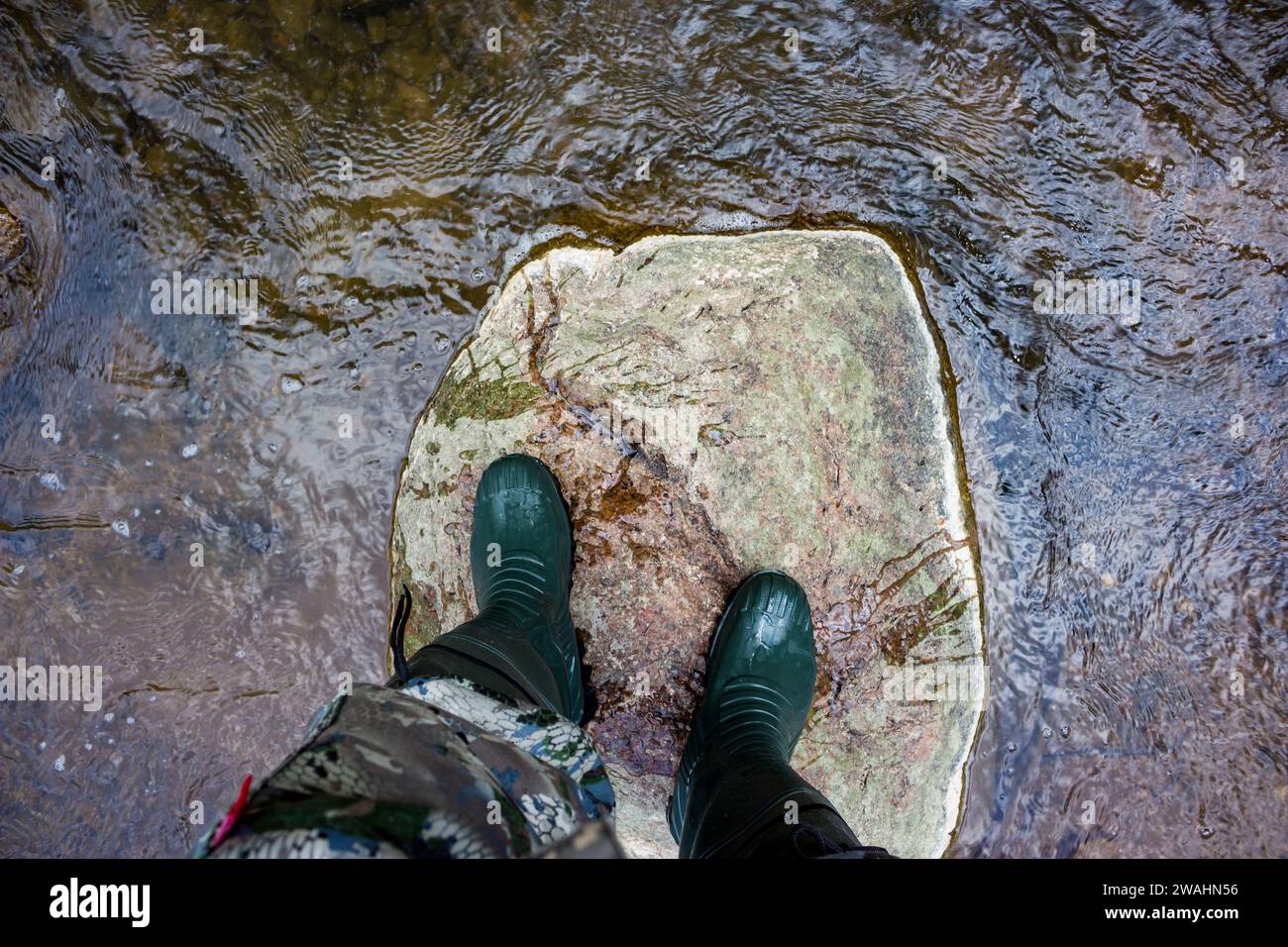 Standing in rubber boots on a large rock in the middle of the river ...
