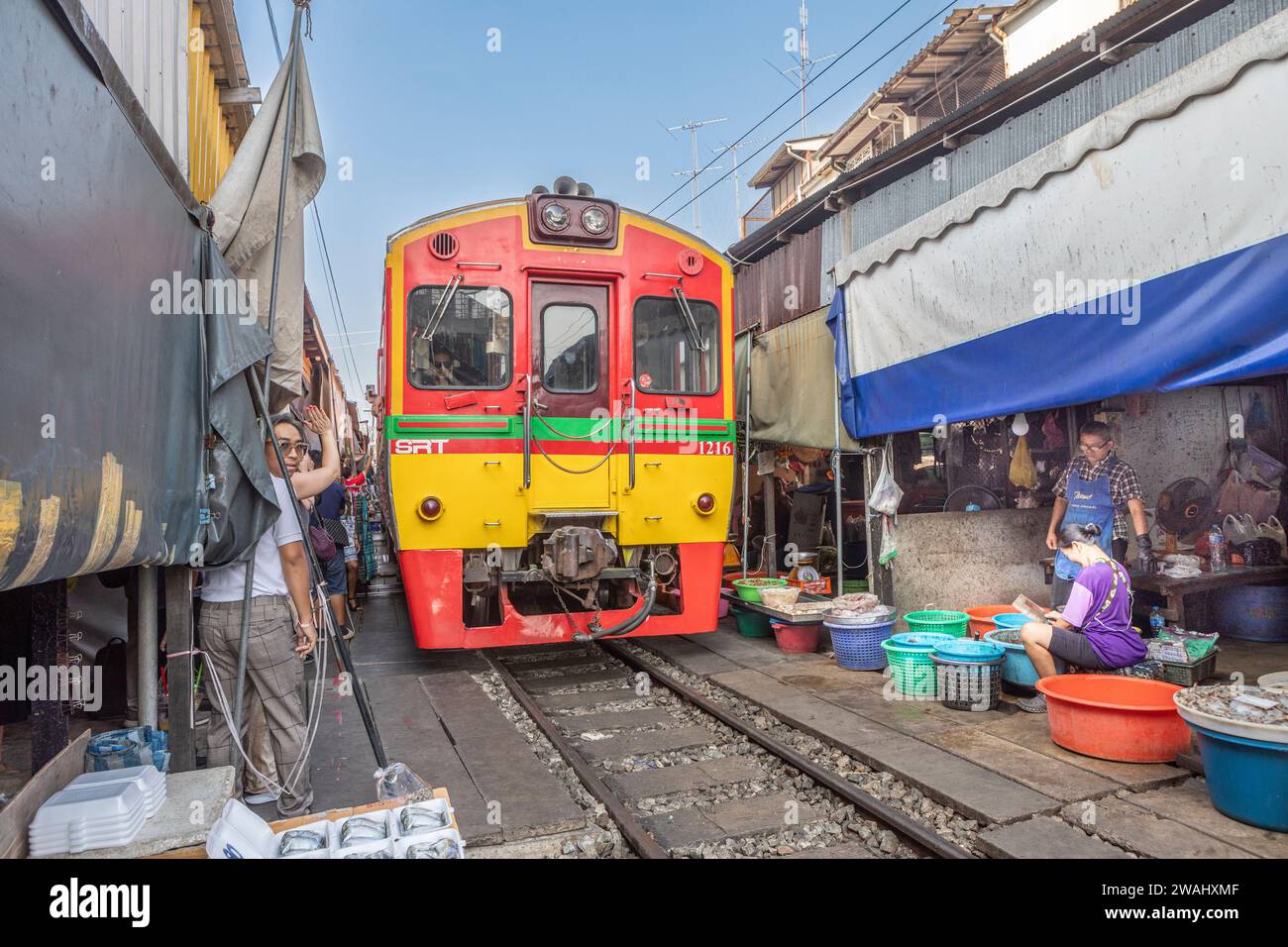 A railway train traveling slowly through Mae Klong Railway Market ...