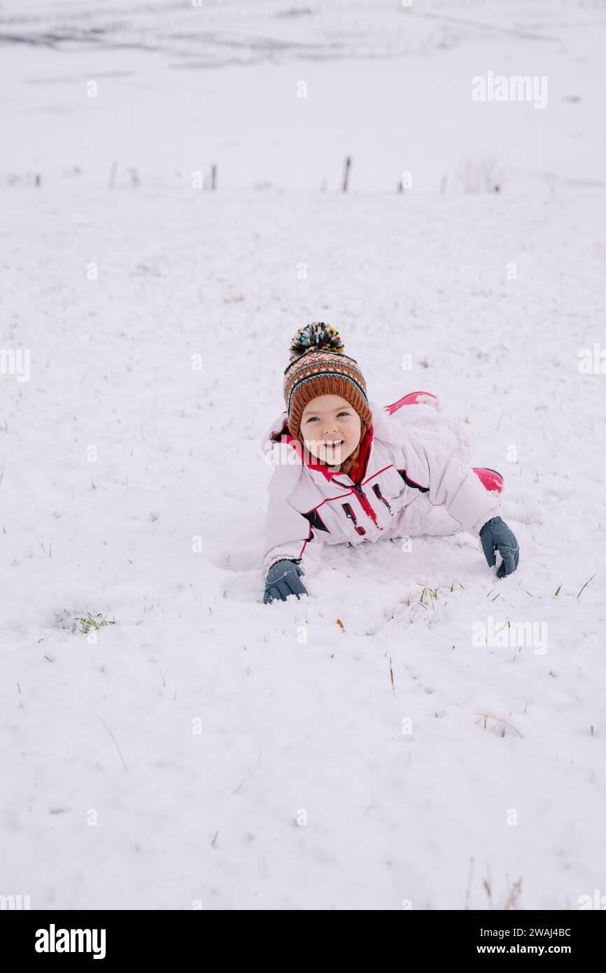 Little smiling girl lying on her stomach in the snow Stock Photo - Alamy