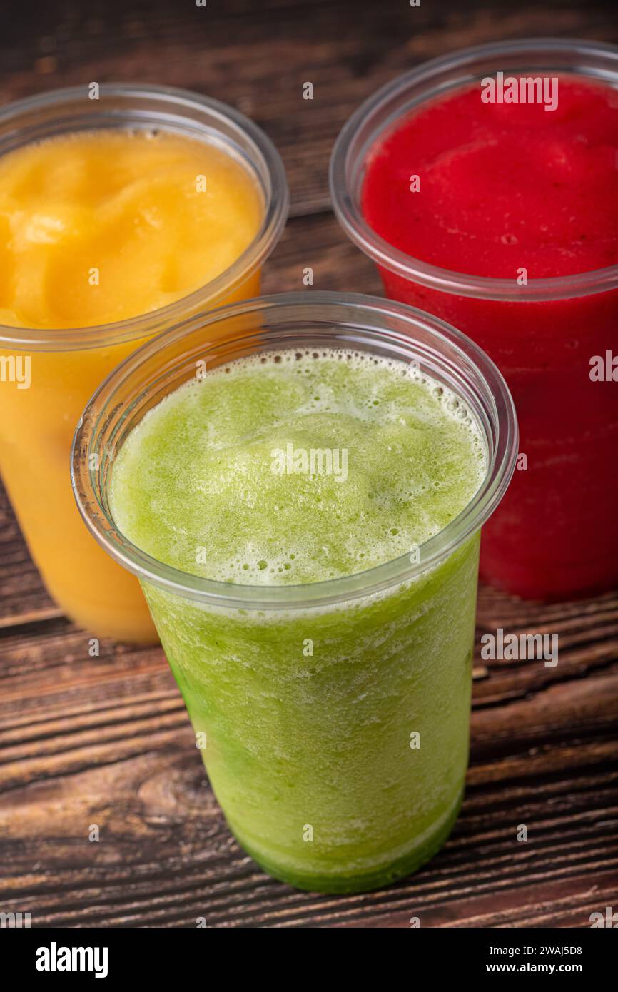 Three different fruit smoothies in plastic take away glasses on wooden ...