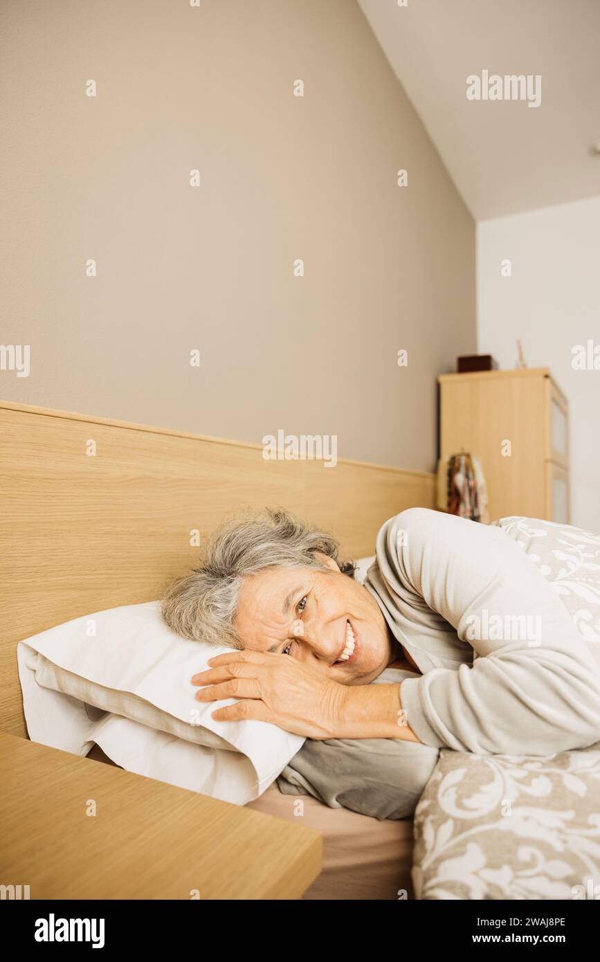 Portrait of a smiling senior woman in her bed in the early morning ...