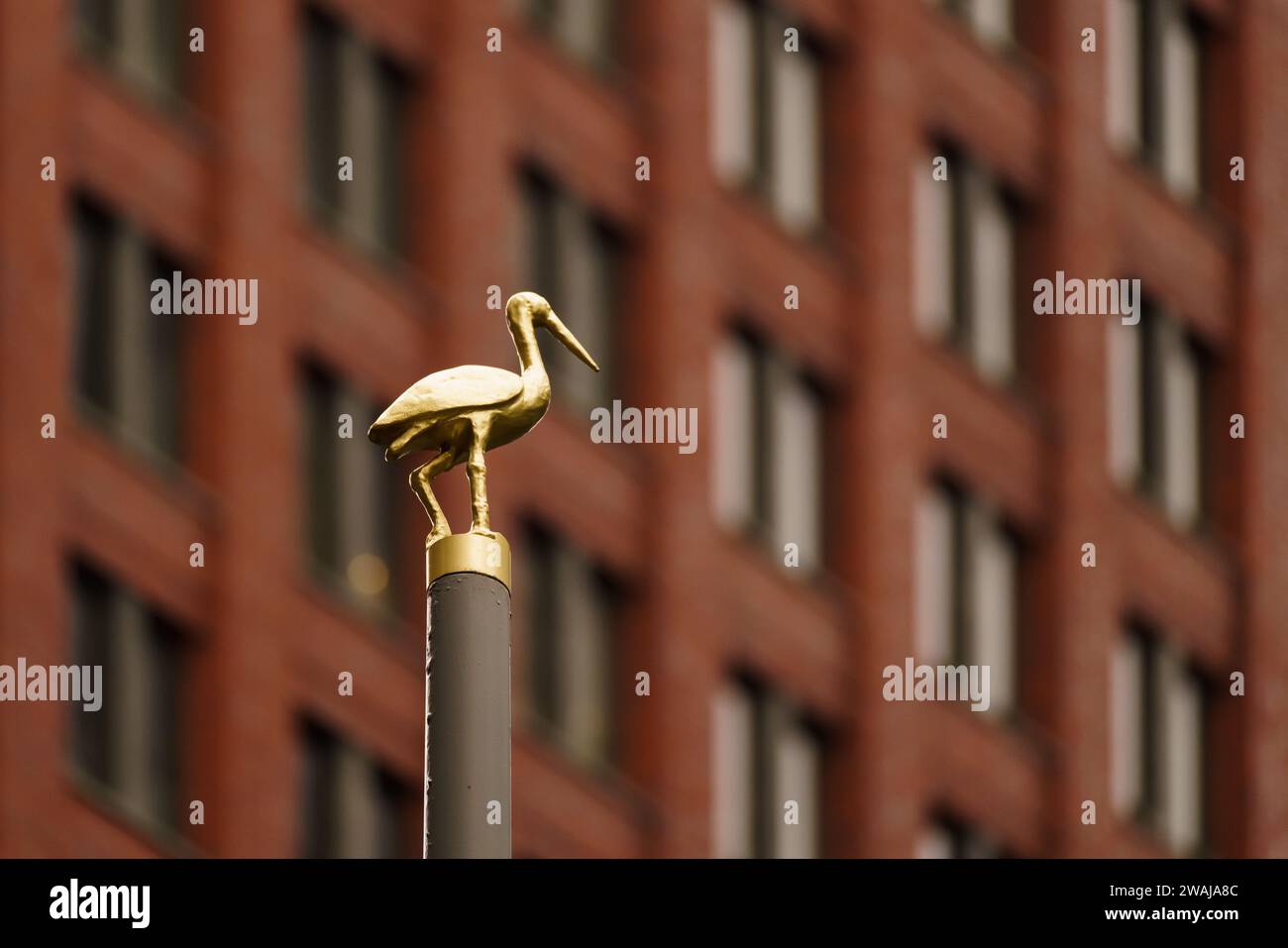 Golden stork sculpture atop a post with a blurred background of brick ...