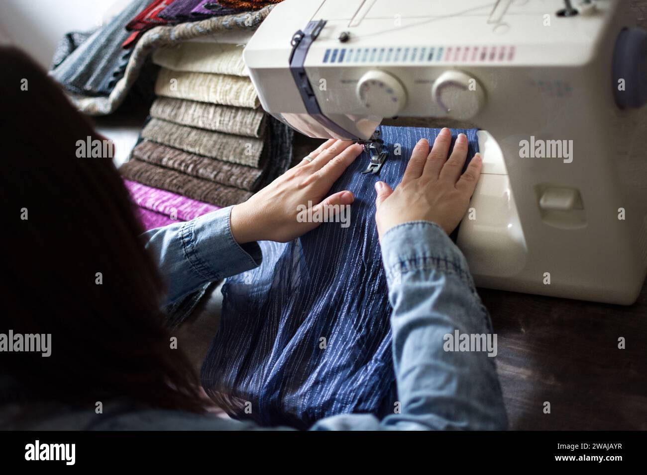 A person is seen sewing a piece of denim fabric on a white sewing ...