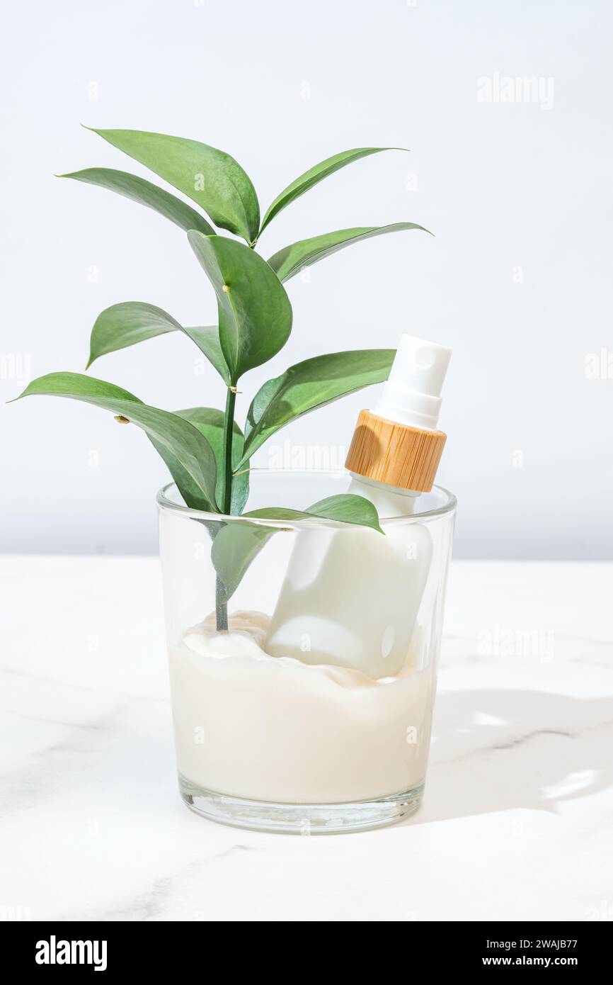 A skincare serum bottle placed in a glass beaker with a natural leaf ...