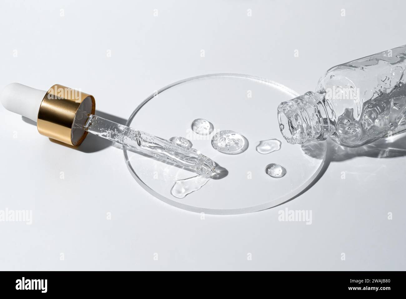 A luxurious serum dropper and glass bottle spilling clear fluid on a ...