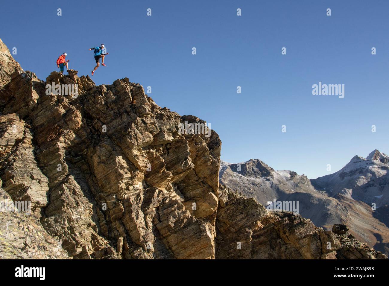 From below of two trail runners leaping across a gap on a rugged cliff ...