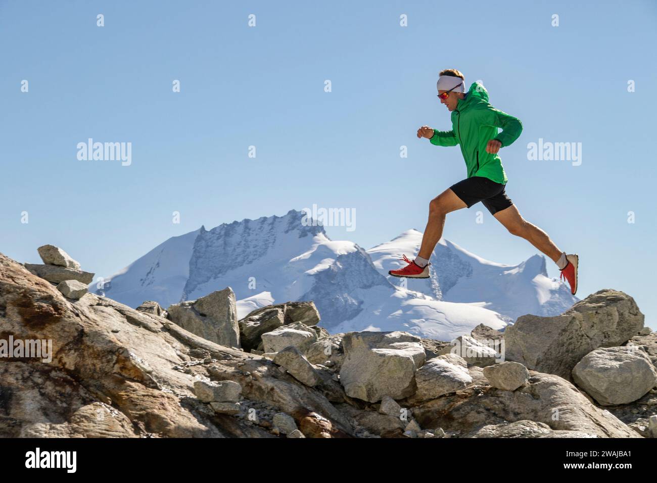 Full body of runner in a green jacket leaping between rocks with snowy ...
