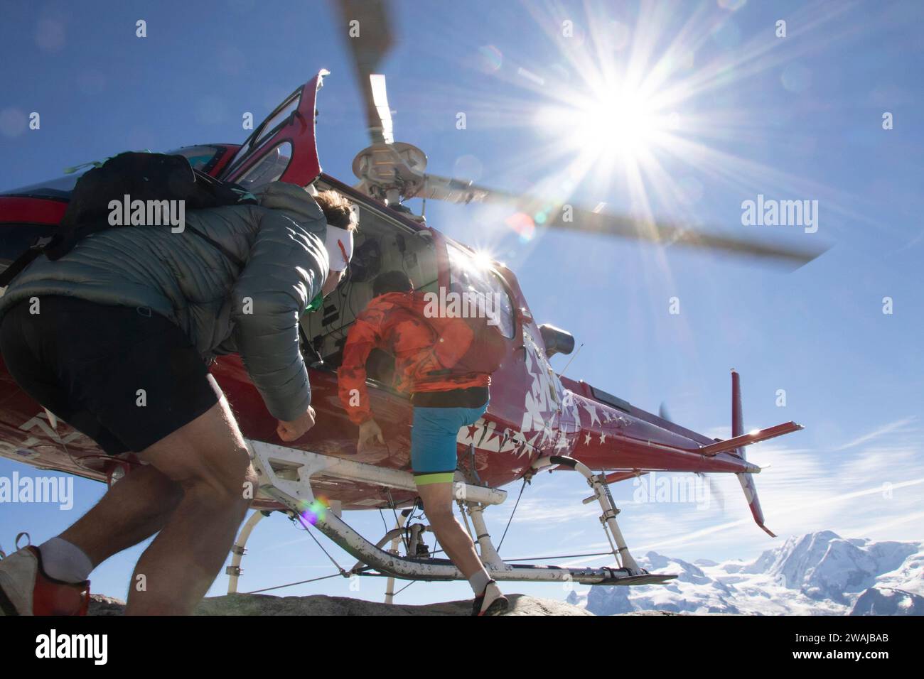 From below of anonymous skiers boarding a rescue helicopter on a bright sunny day in the high ...