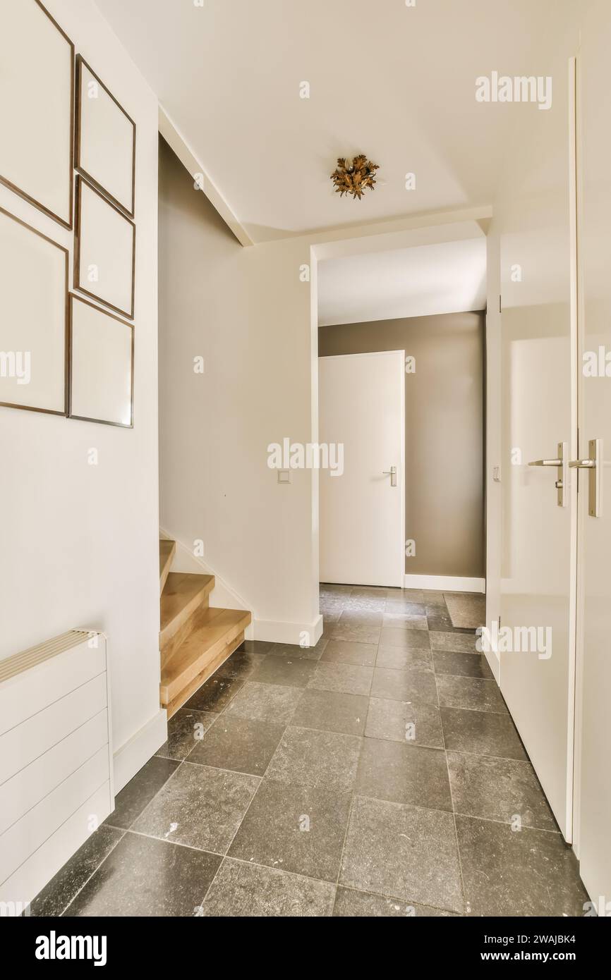 Interior of empty tiled hallway with stairs and white frames on wall at ...
