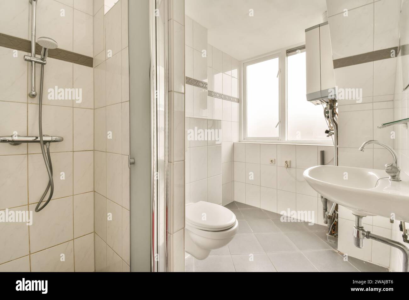 Shower booth with toilet seat and sink in bathroom with bright window ...
