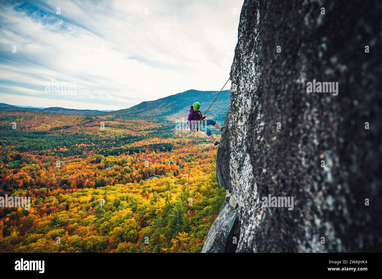 Woman rappelling/abseiling down rock face during foliage in afternoon ...