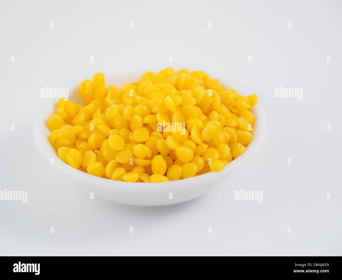 A bowl full of natural yellow beeswax peals isolated on a white ...