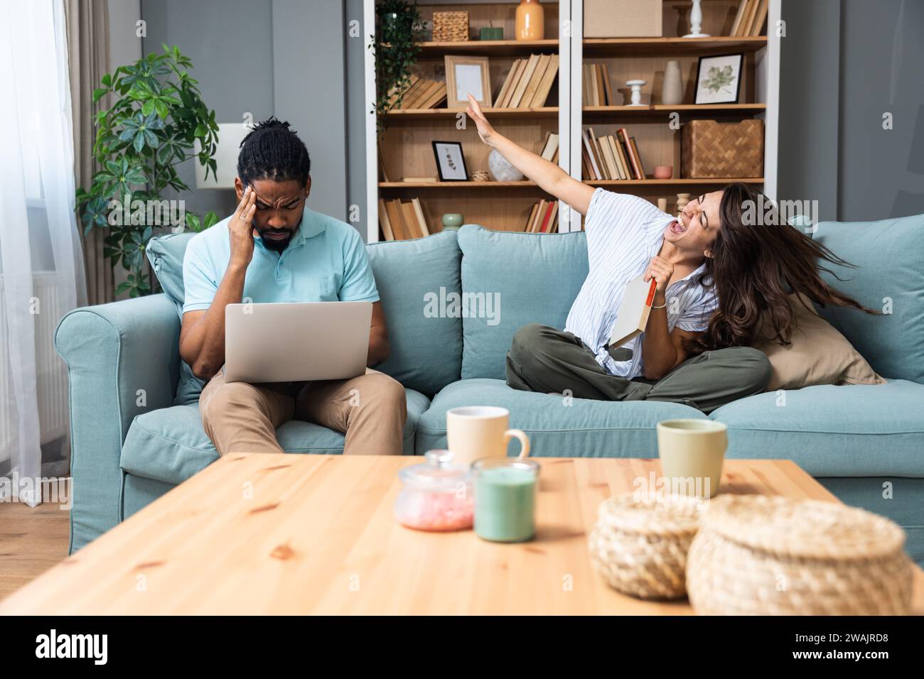 Young woman having fun and trying to distract her boyfriend working ...