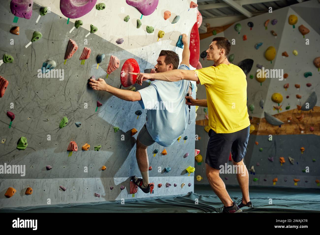 Male instructor teaching man to climb artificial wall. Man training ...