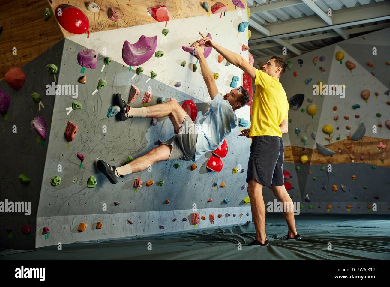 Male instructor teaching man to climb artificial wall. Man training ...