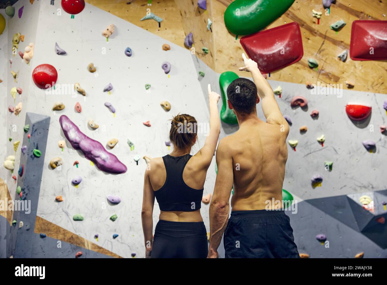 Young man and woman, athletes looking on climbing wall, discussing ...