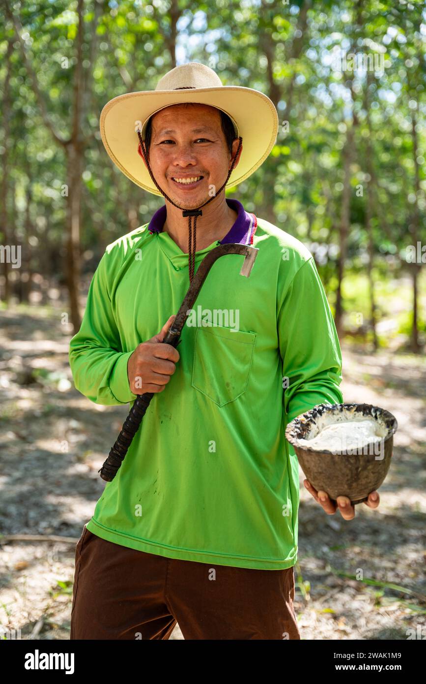 Portrait of smiling asian rubber farmers stand holding cups of latex in ...