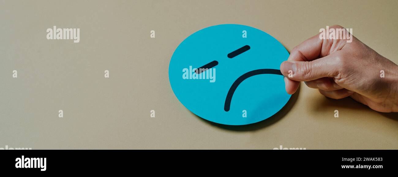 man setting a sad mouth in a blue cardboard face on a yellow background ...