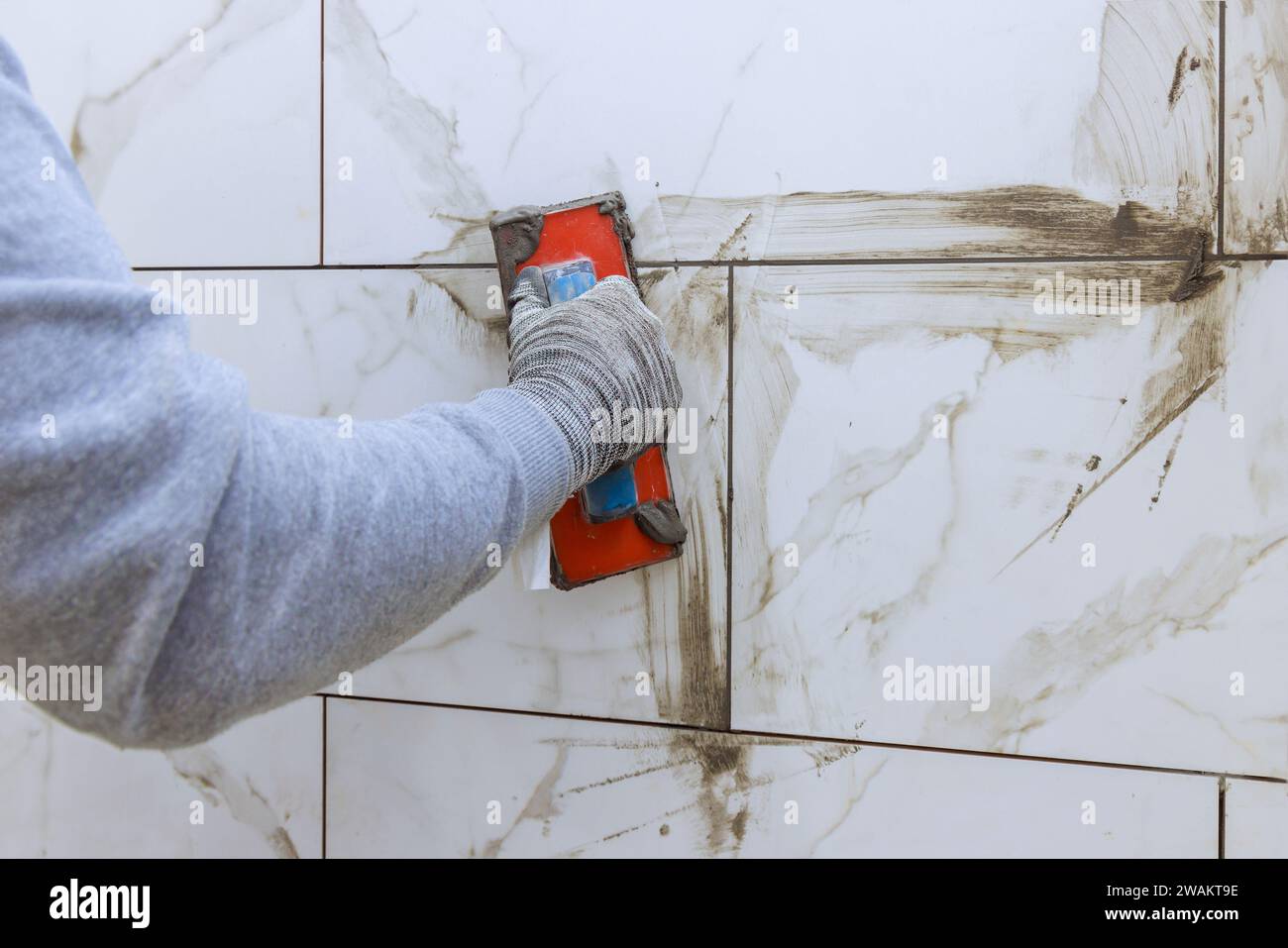 An grouting process, tilers use rubber trowels to fill in spaces ...