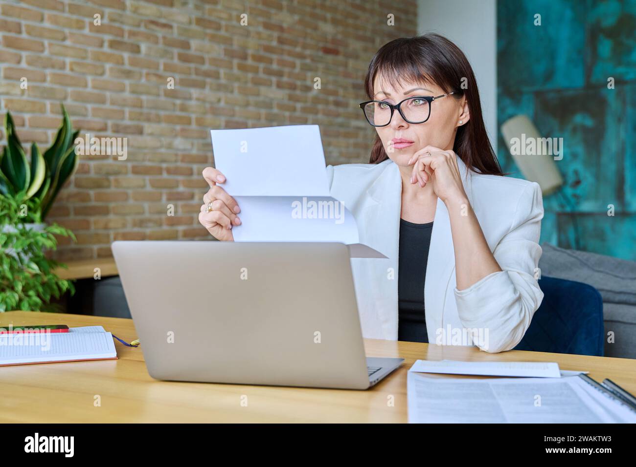 Serious mature businesswoman reading official letter, sitting in office ...