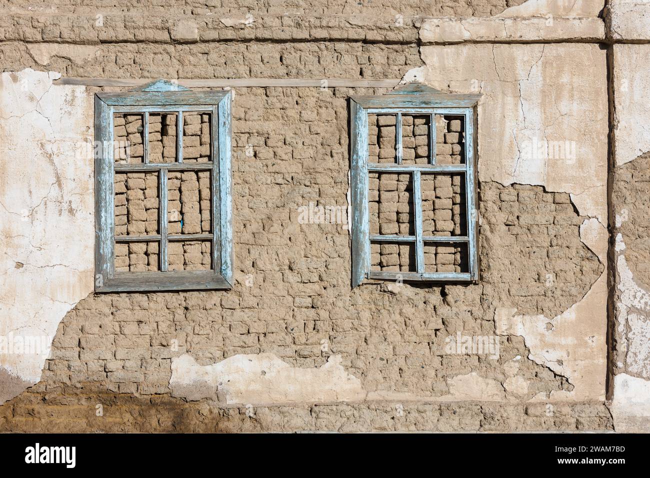 old house adobe air brick wall with two embedded wooden window frames ...