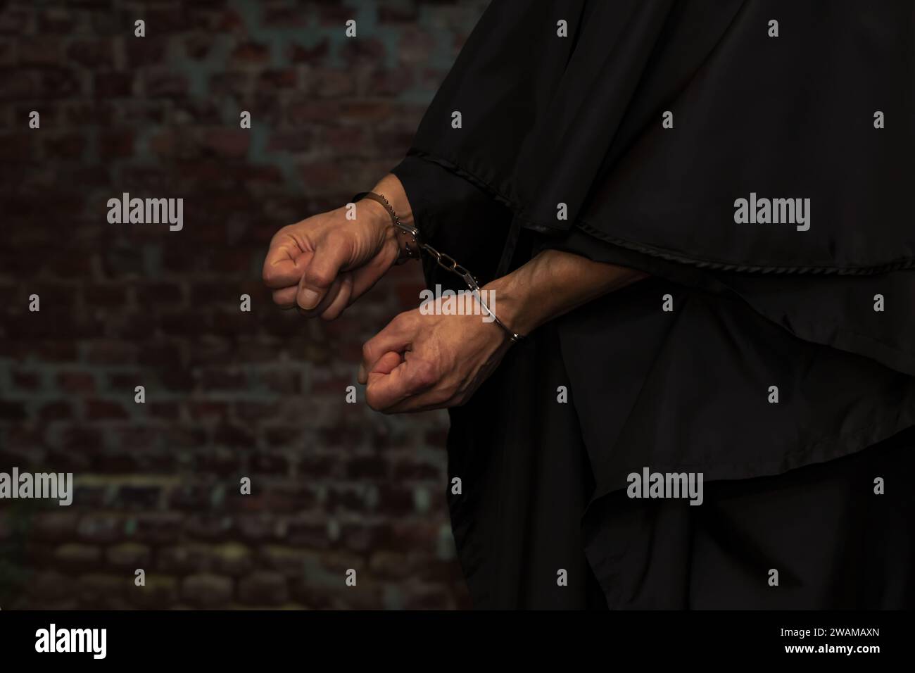 The hands of a monk or priest in handcuffs on the background of a stone ...
