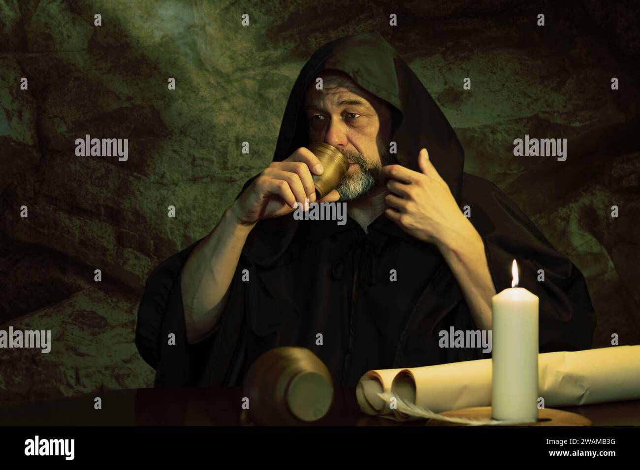 Monk in black cassock drinking wine from clay goblet sitting at table ...