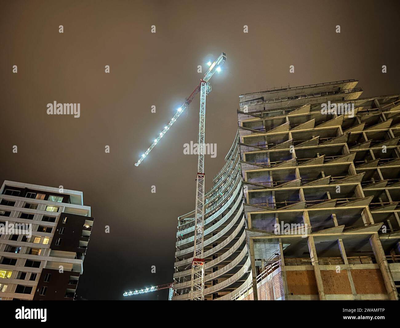 Illuminated tower crane builds a large multi-storey building against a ...