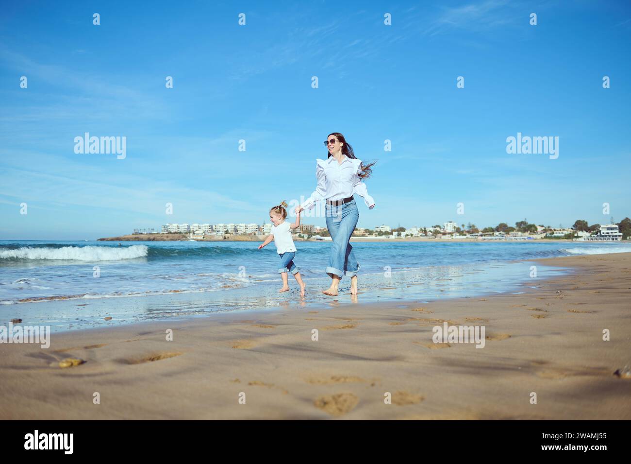 Caucasian young mother and daughter holding hands, running barefoot on ...