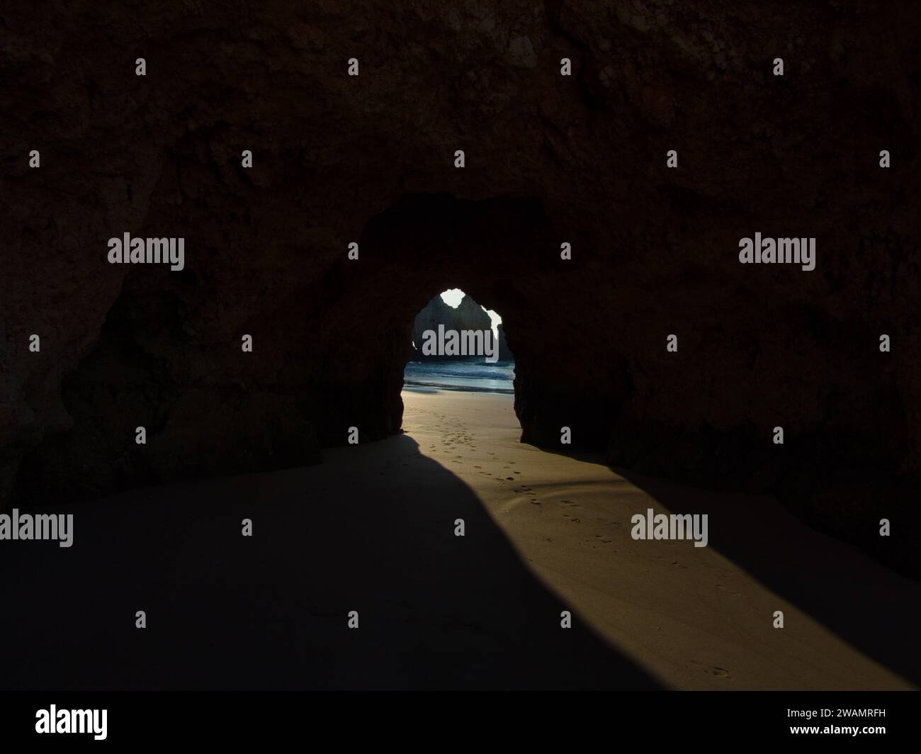 Ray of light entering a dark cave on the beach leaving a path of light ...