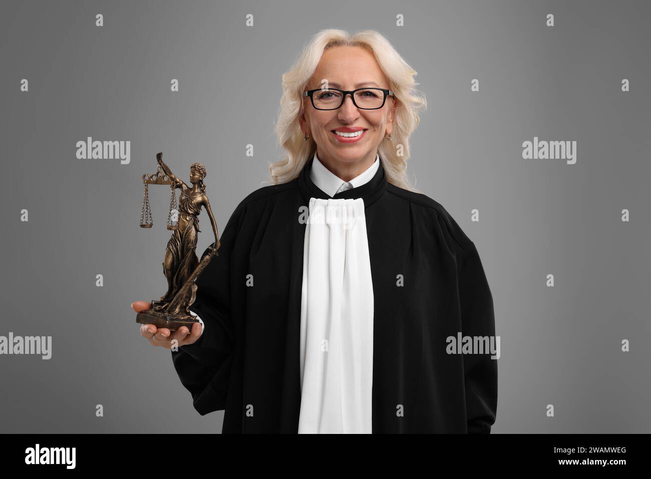 Smiling senior judge with figure of Lady Justice on grey background ...