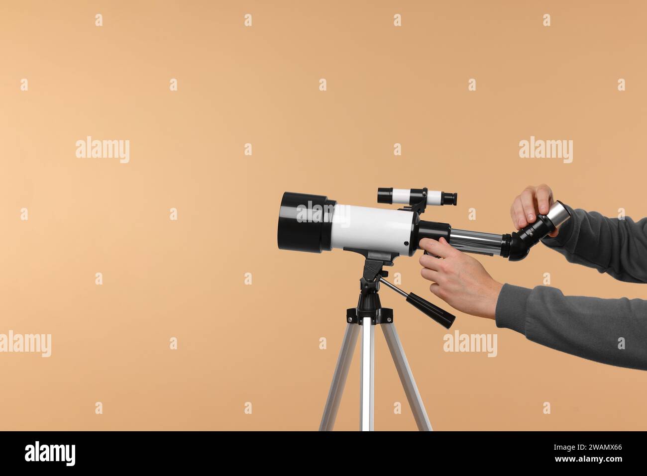 Astronomer setting up telescope on beige background, closeup. Space for ...