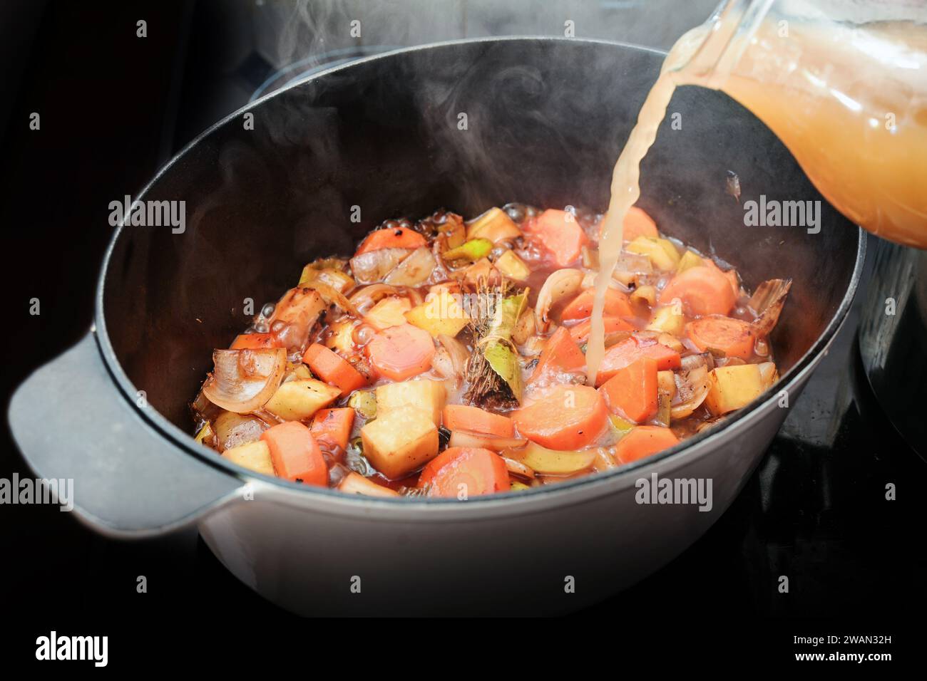 Homemade broth is poured into a casserole pot to deglaze steaming ...