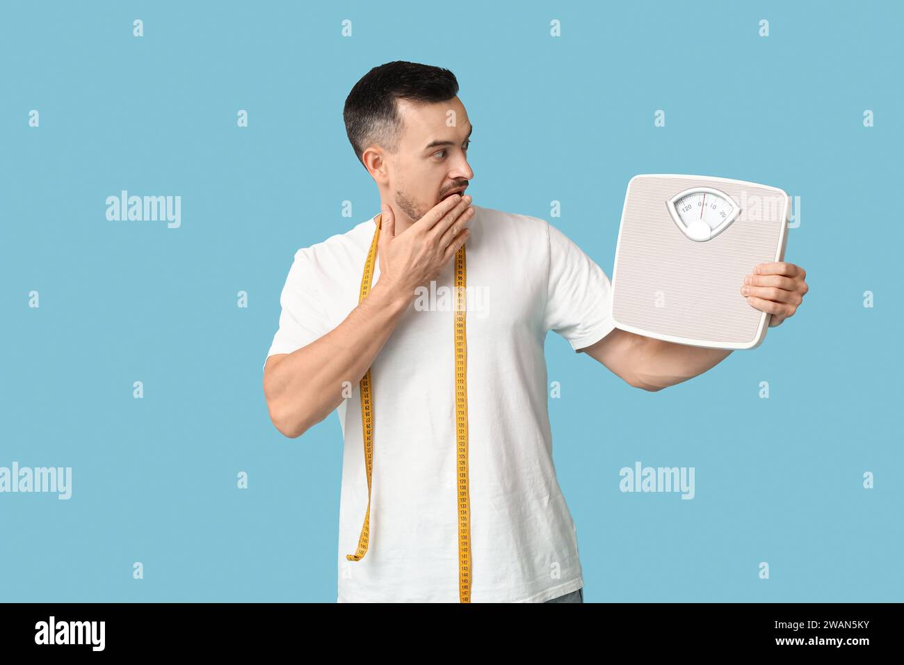 Handsome sporty shocked man with measuring tape and scales on blue ...