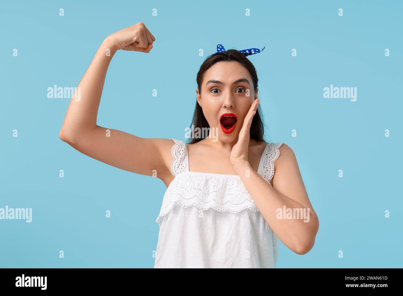 Beautiful surprised pin-up woman showing her muscles on light blue ...