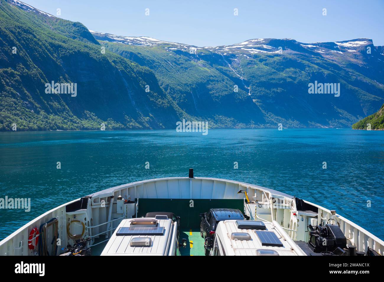 A ferry navigates the waters of Geirangerfjord between the villages of ...