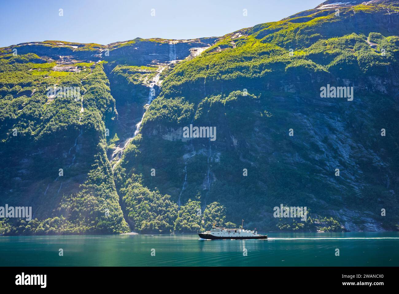A ferry navigates the waters of Geirangerfjord between the villages of ...