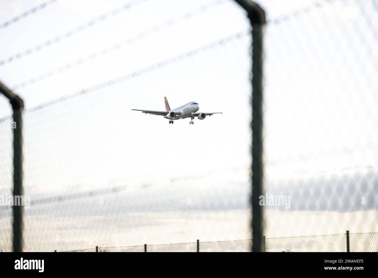 A passenger plane seen from behind a fence approaching to land on an ...