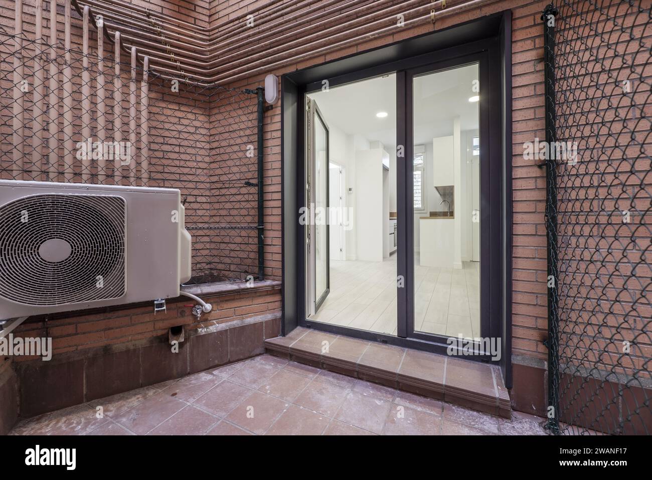 A small interior patio with an air conditioning compressor, brick walls ...