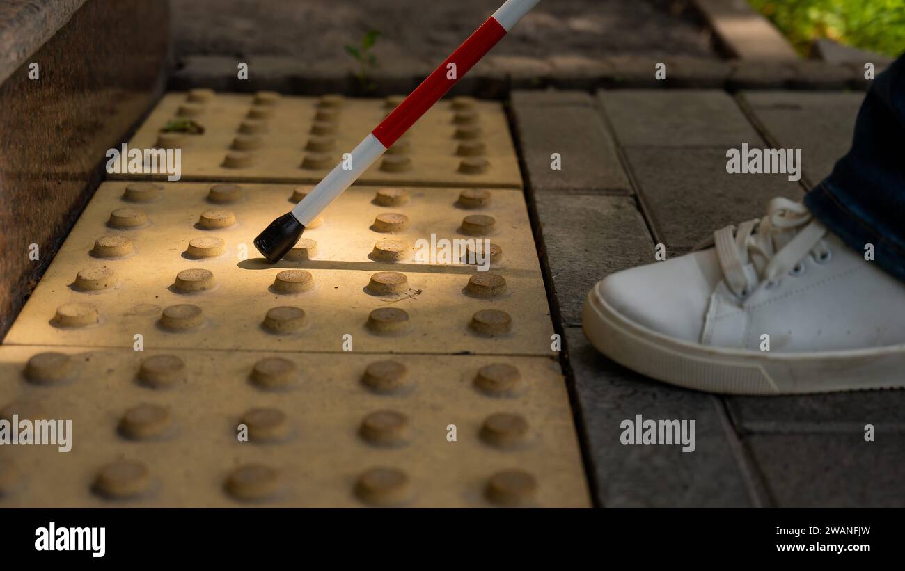 A close-up of a woman's feet with a tactile cane and a tactile tile ...