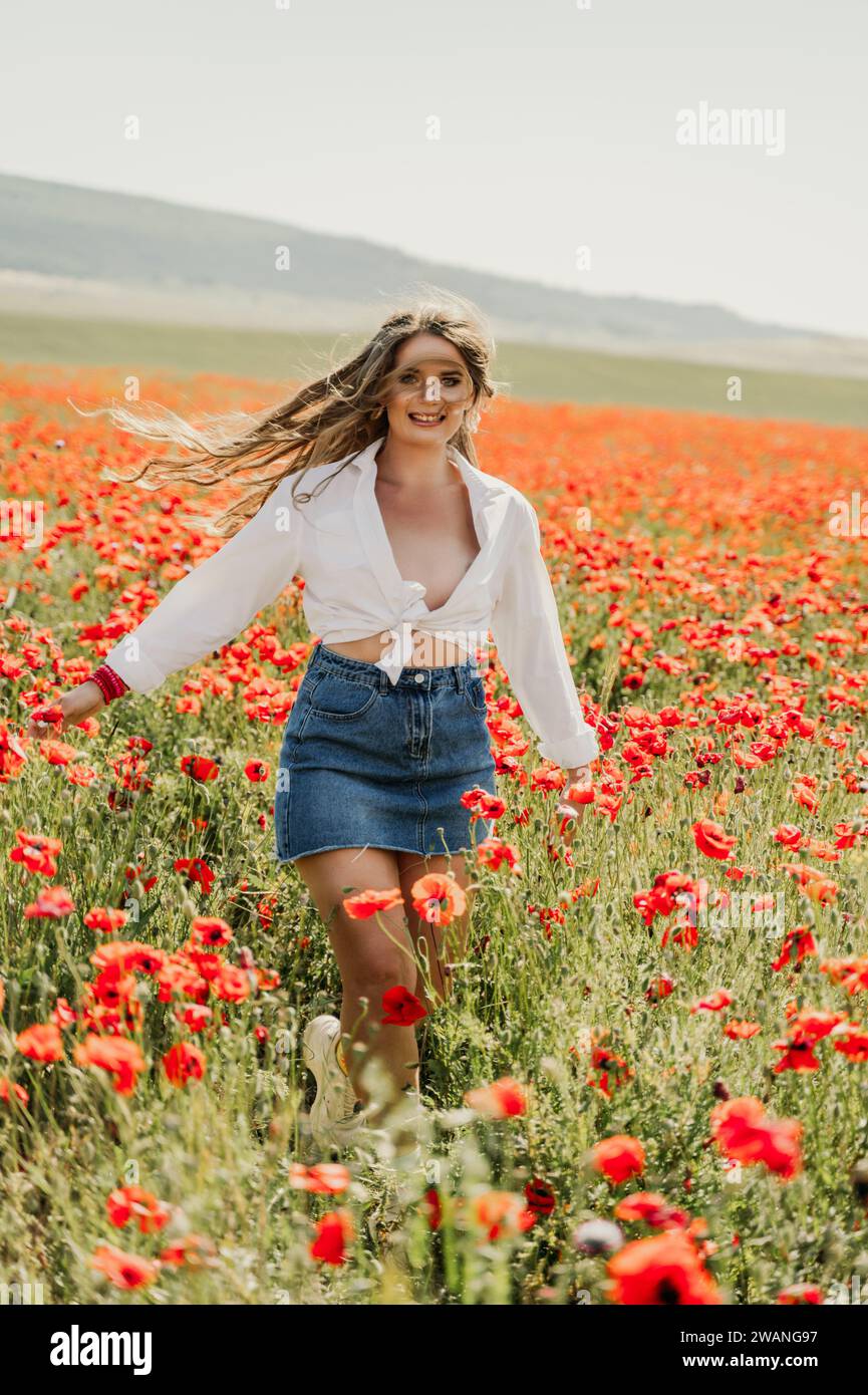 Happy woman in a poppy field in a white shirt and denim skirt with a ...