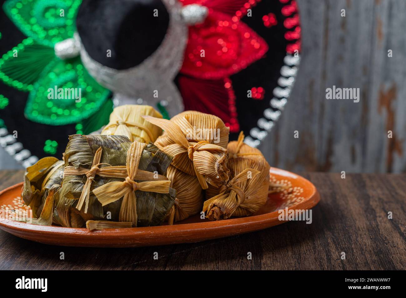 Different tamales in a clay dish on a wooden table. Background with ...