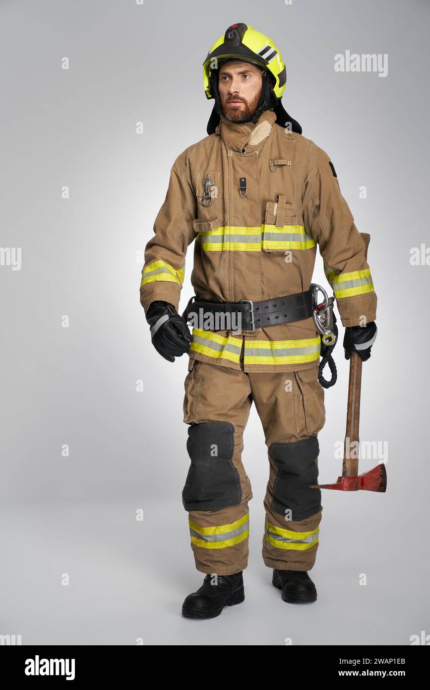 Focused firefighter in full gear with axe walking indoors. Front view ...