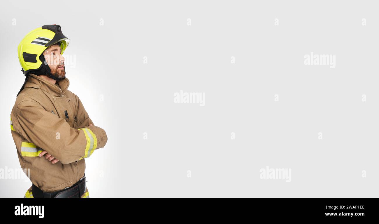 Serious fireman in protective helmet looking up and away on copy place ...