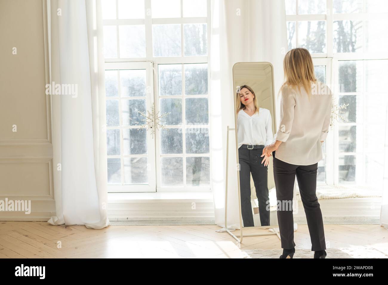 Self-confident Woman looking at her reflection into the mirror indoors ...