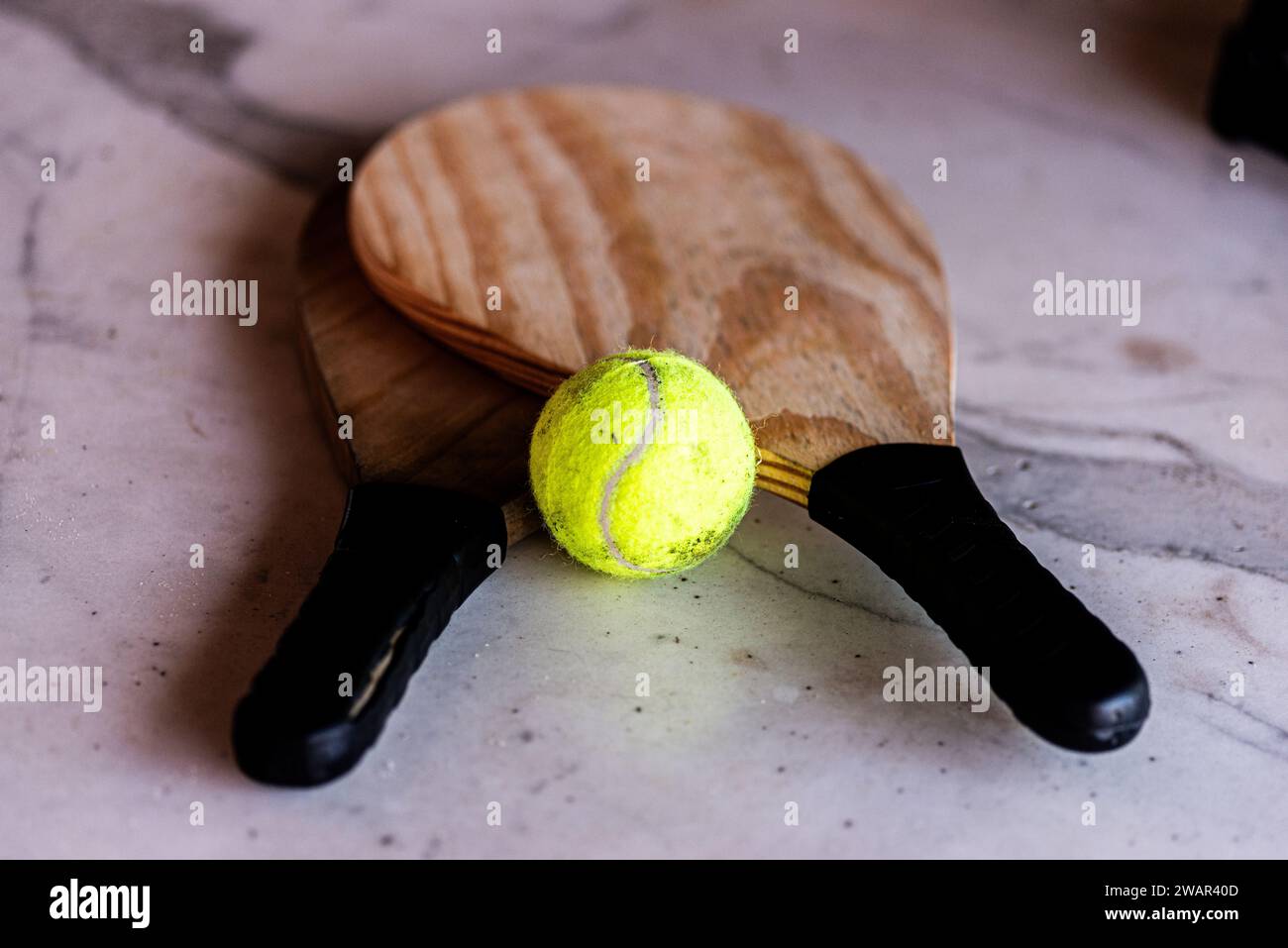 A well-worn tennis racket and ball sit on a hardwood floor, the bright ...
