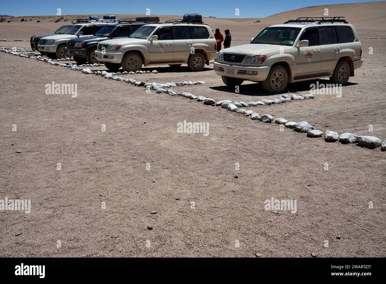 4x4 vehicles in the desert with mountains behind under a blue sky ...