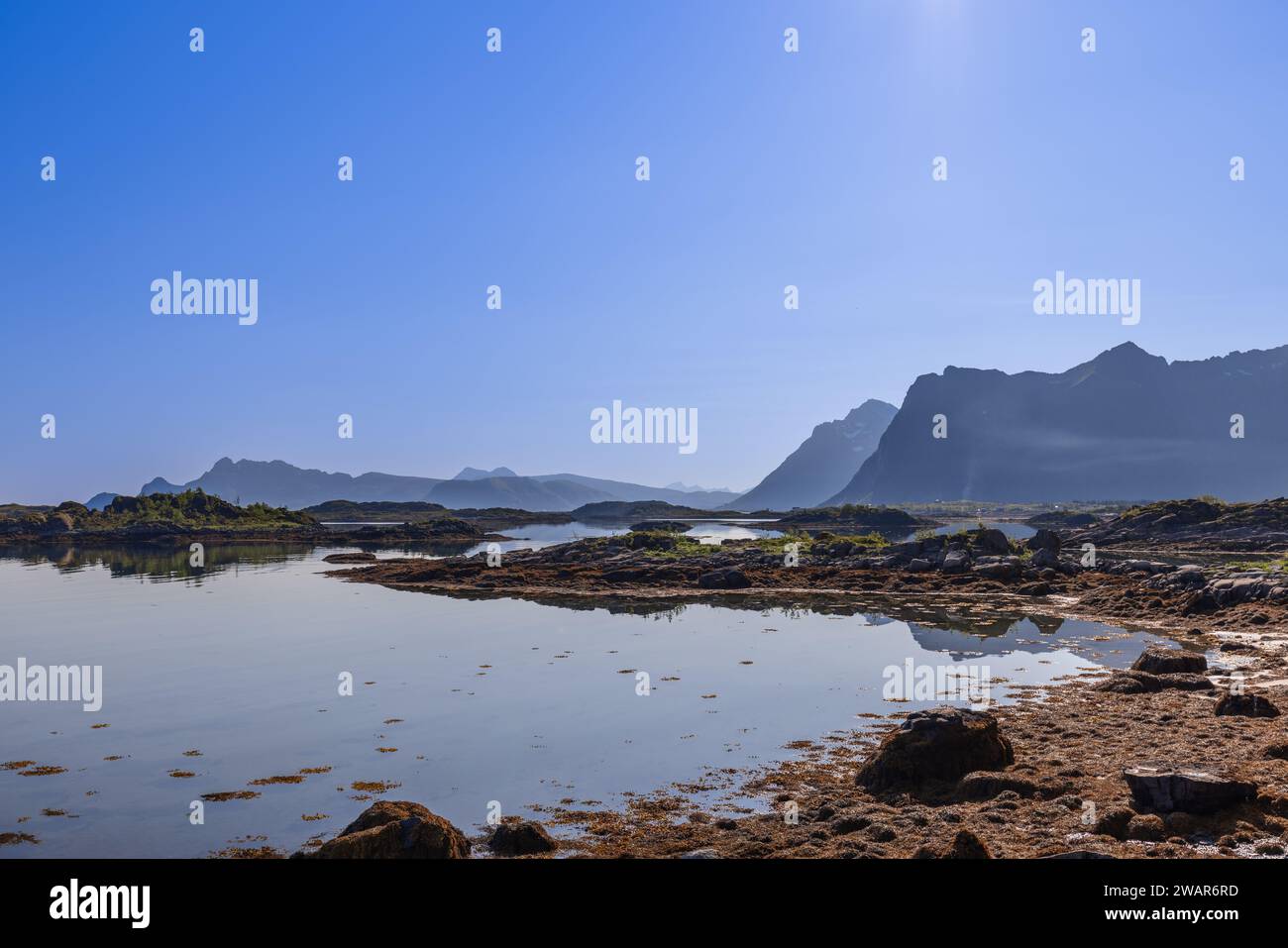 A serene Norwegian coastal landscape featuring a calm inlet with rocky ...